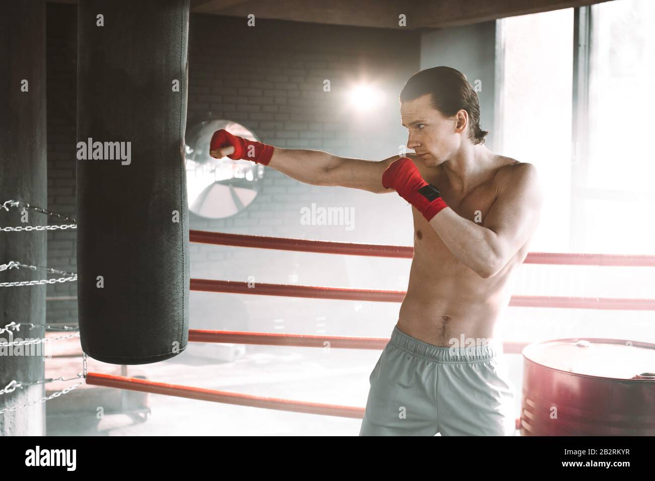 angry boxer standing in boxing pose near punching bag on black with ...