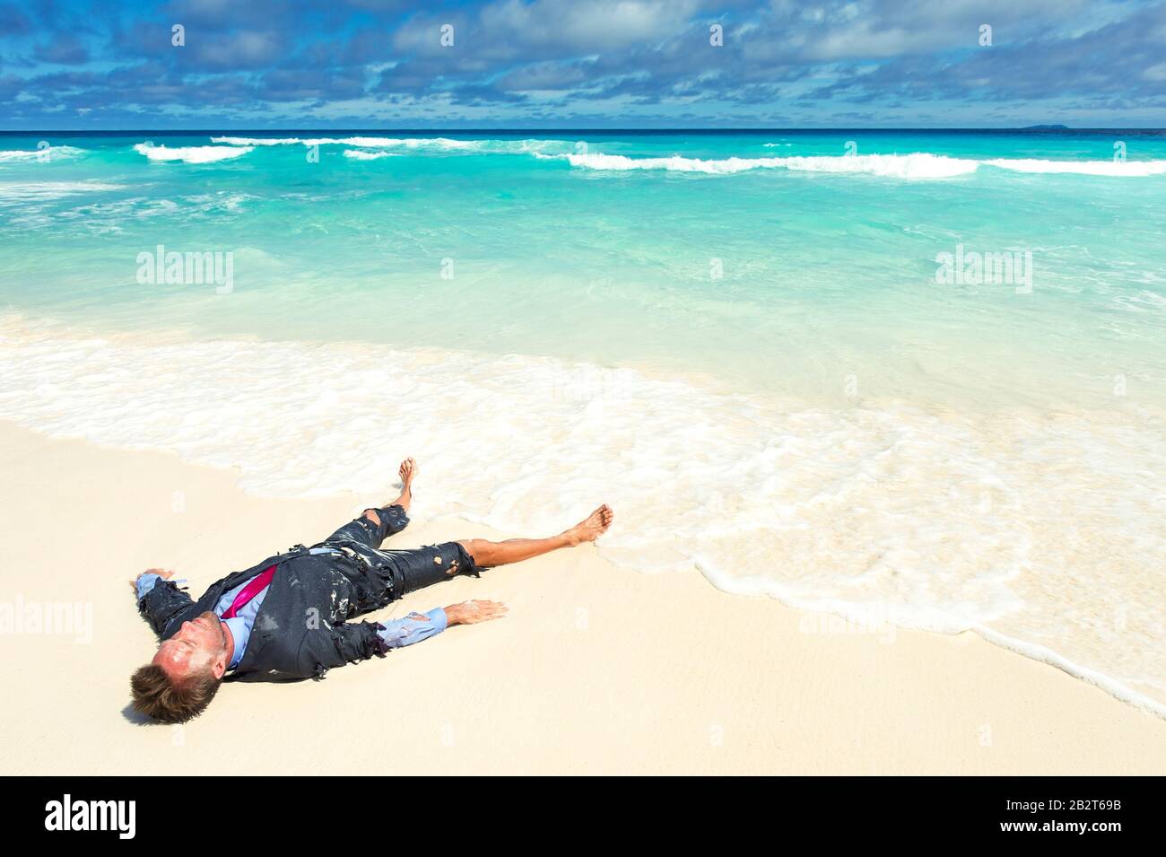 Castaway office worker washed up on a tropical beach in a ragged torn ...