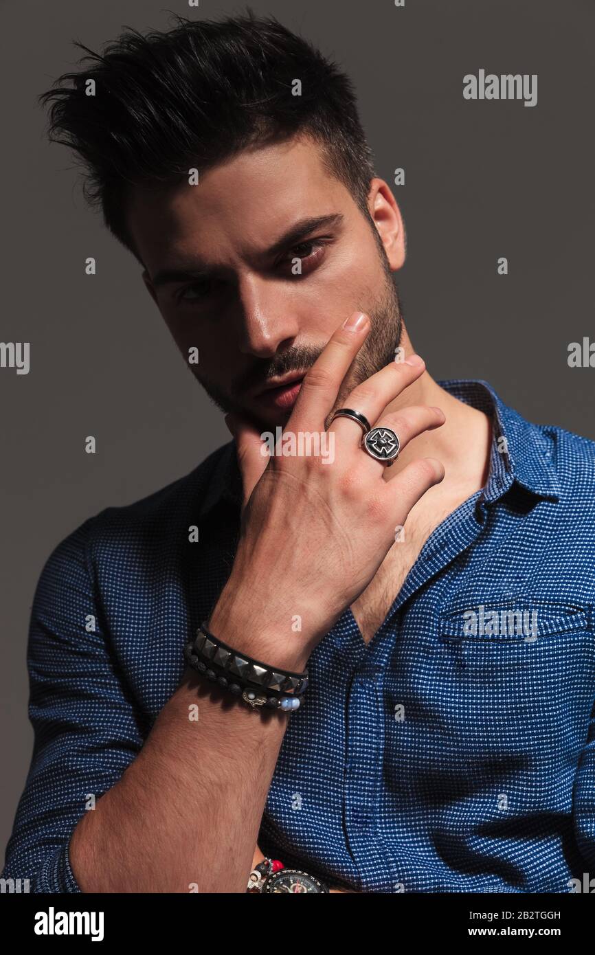 serious fashion man holding chin in his hand thinking on grey ...