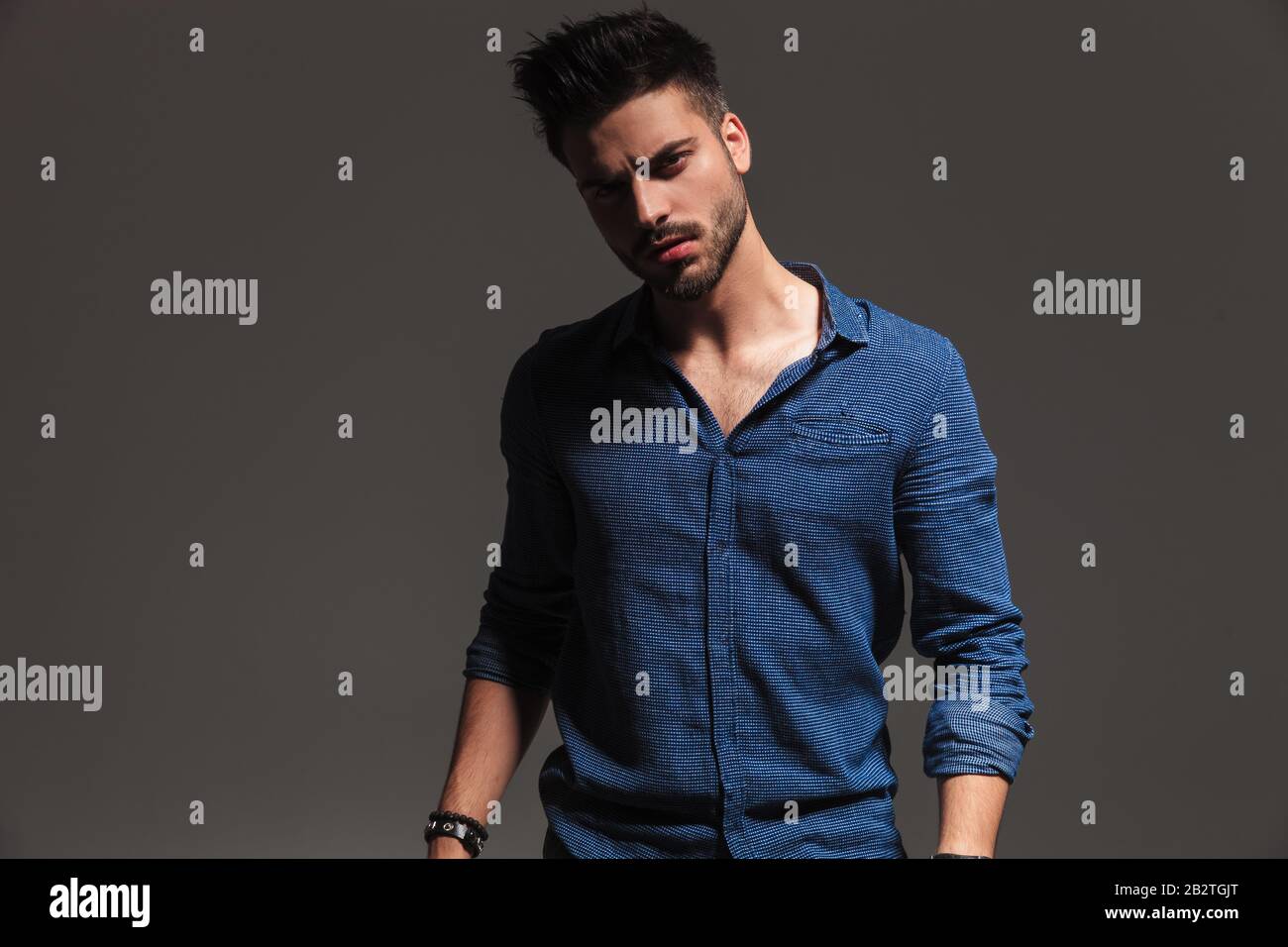 young dramatic man with serious look, standing on grey studio ...
