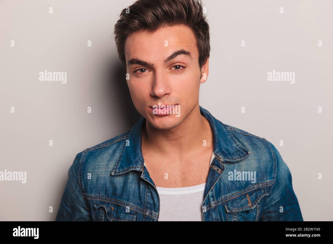 face of a young man in jeans jacket on grey wall Stock Photo - Alamy