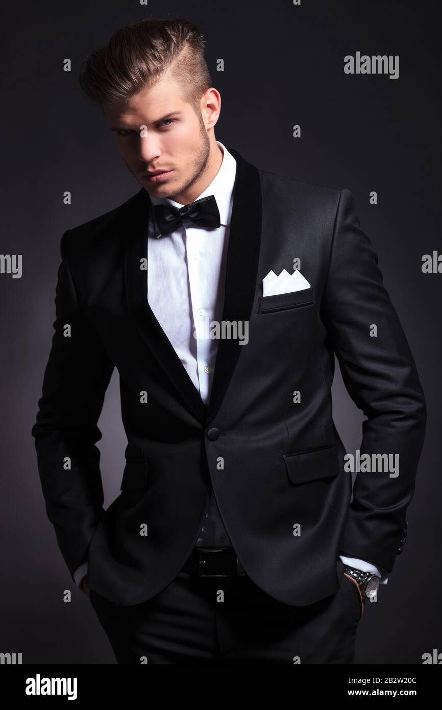elegant young fashion man in tuxedo with half shaded face and hands in ...