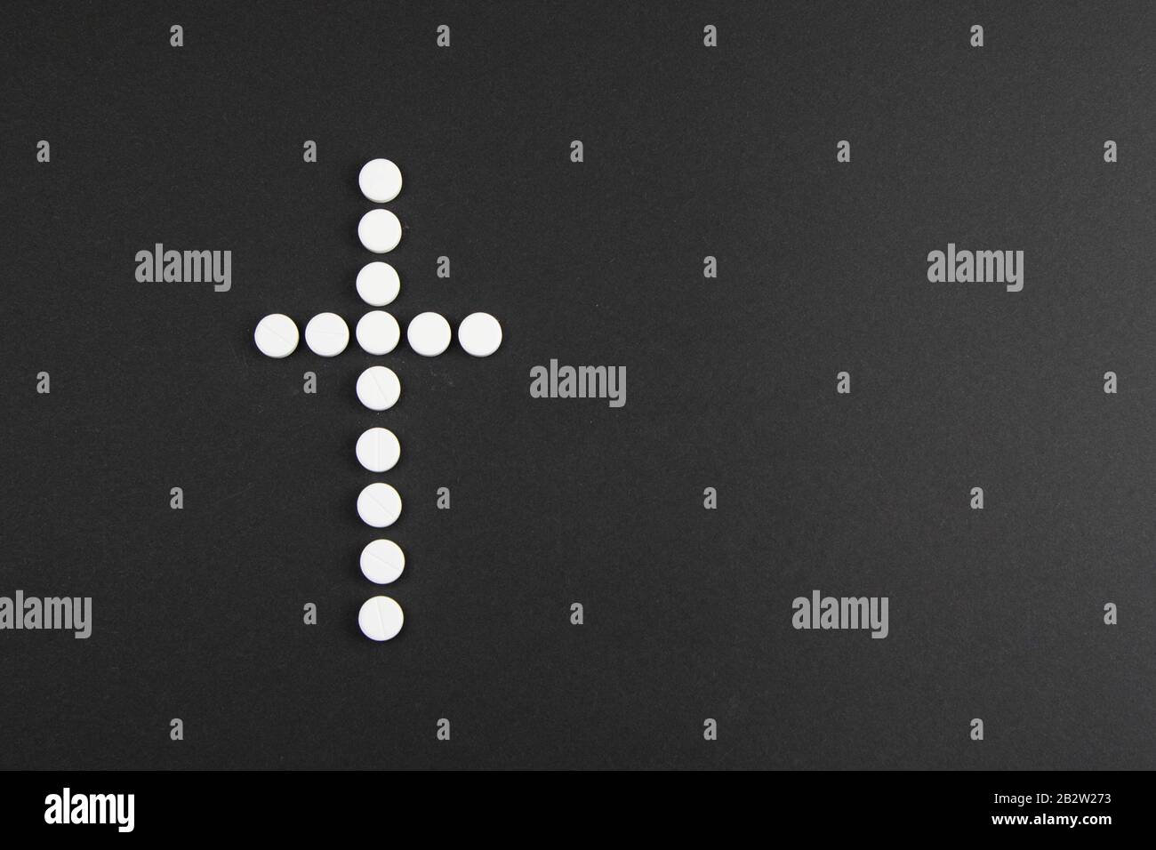 White pills laid out in the shape of a cross on a black background ...