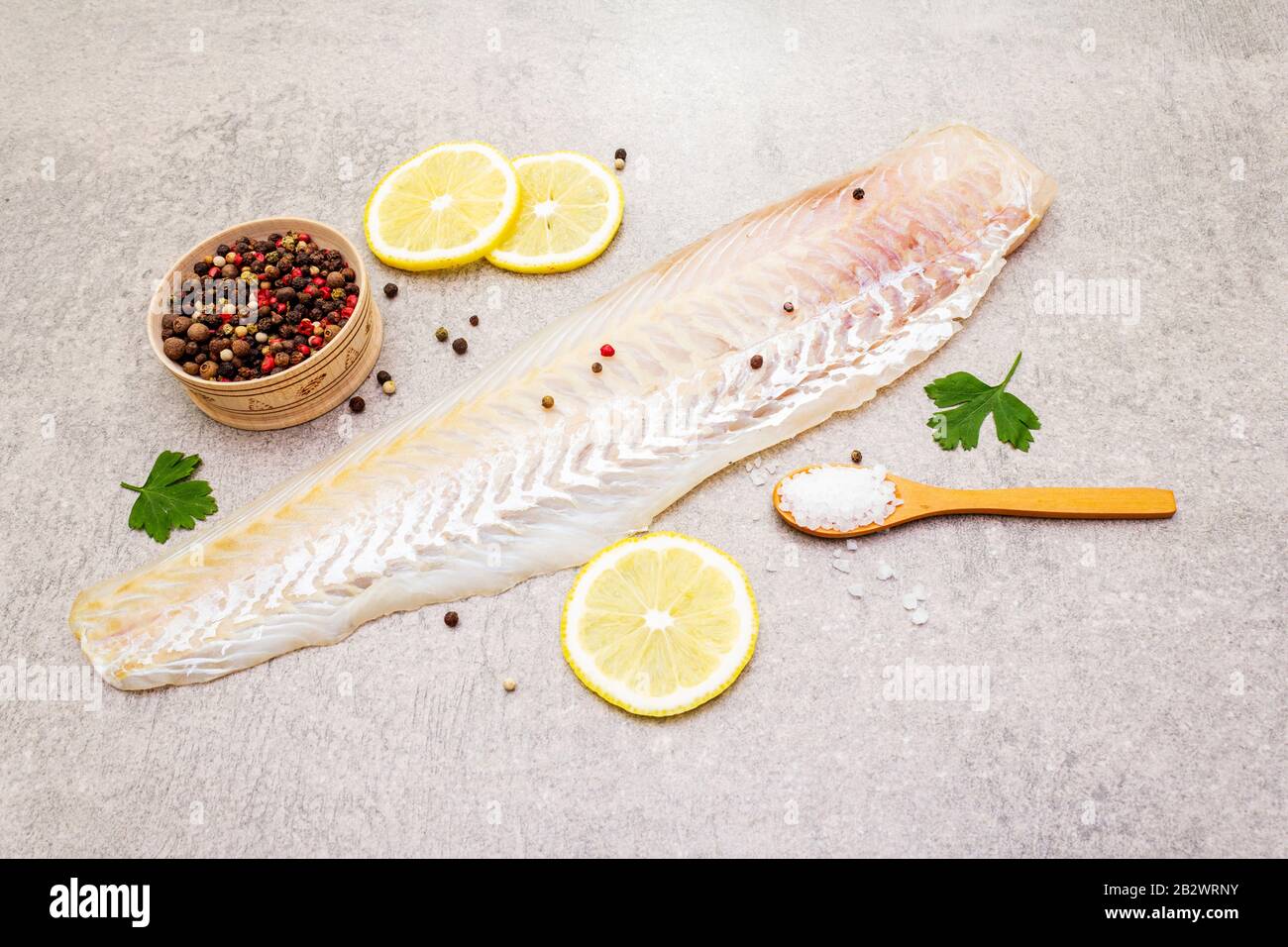 Fresh raw hake fillet on a stone background. With lemon, parsley, salt ...