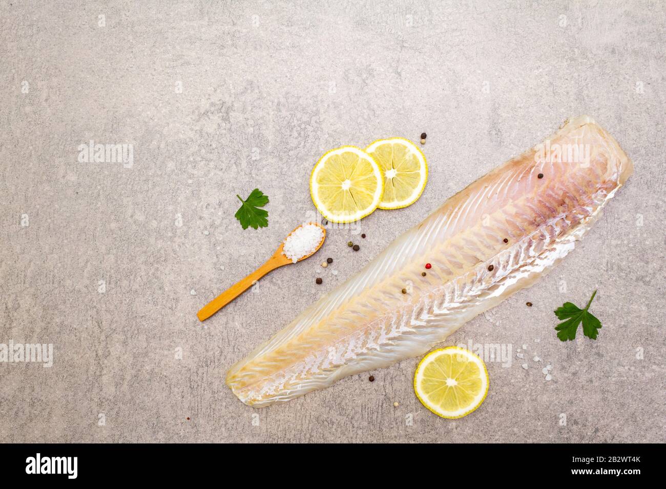 Fresh raw hake fillet on a stone background. With lemon, parsley, salt ...