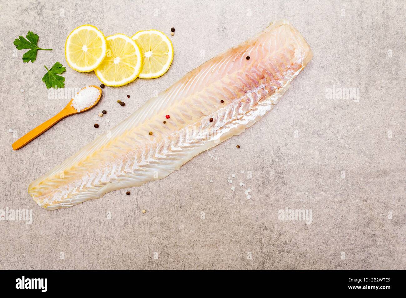 Fresh raw hake fillet on a stone background. With lemon, parsley, salt ...