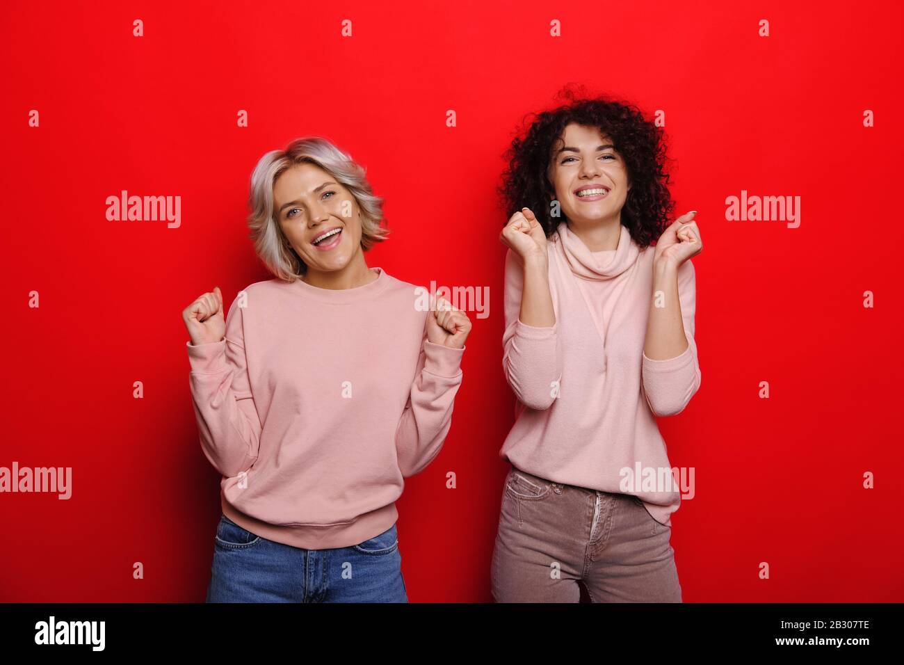 Delight caucasian sisters with curly hair are posing happily on a red ...