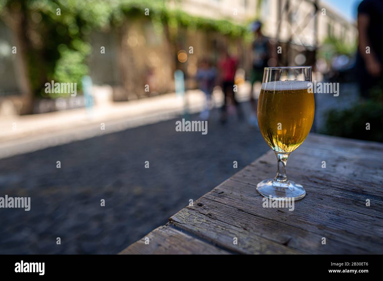 Beer glass sitting on picnic table with people walking by in tourist ...