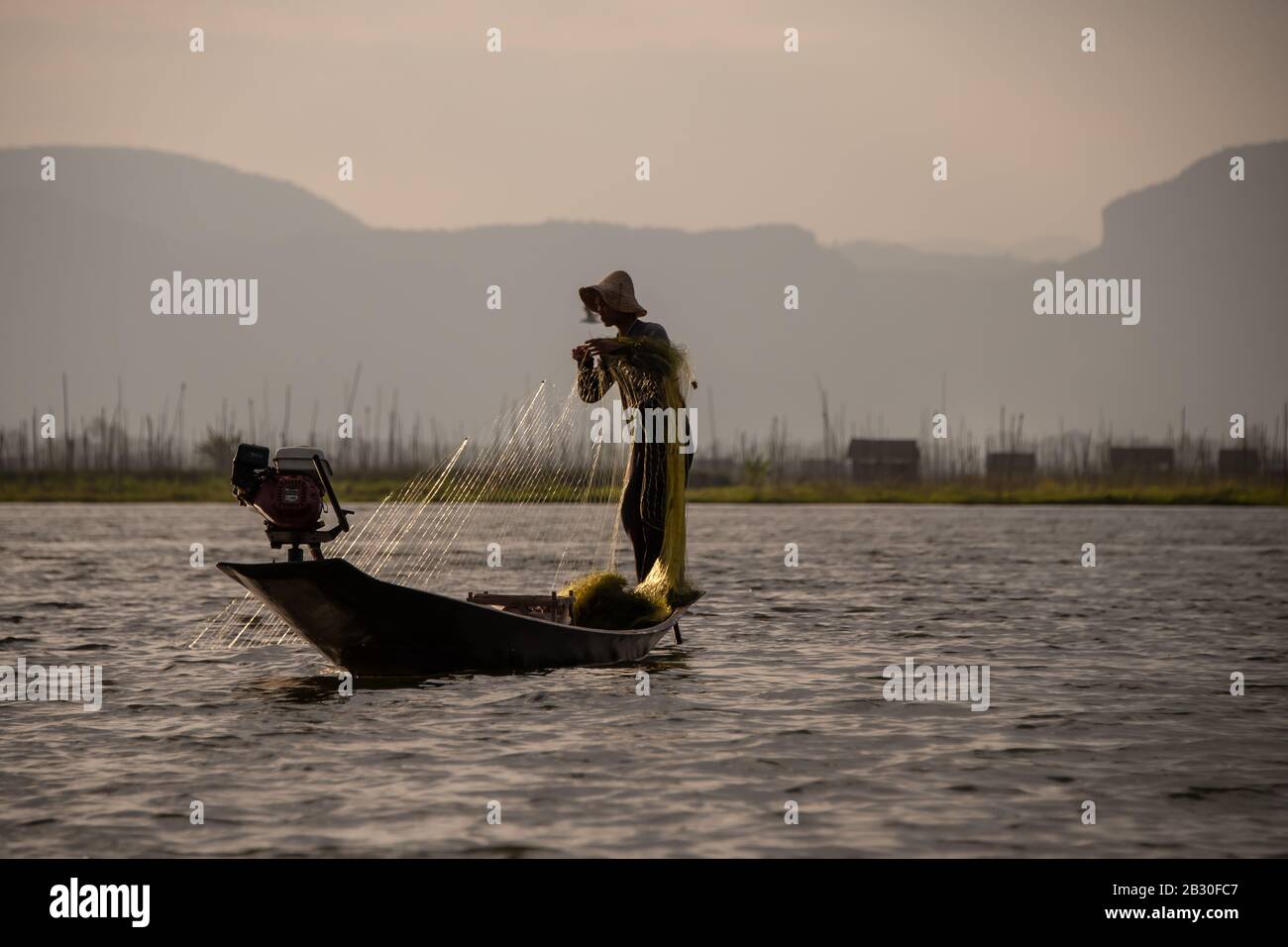 Traditional Intha leg-rowing fisherman with a cast net, illuminated by ...