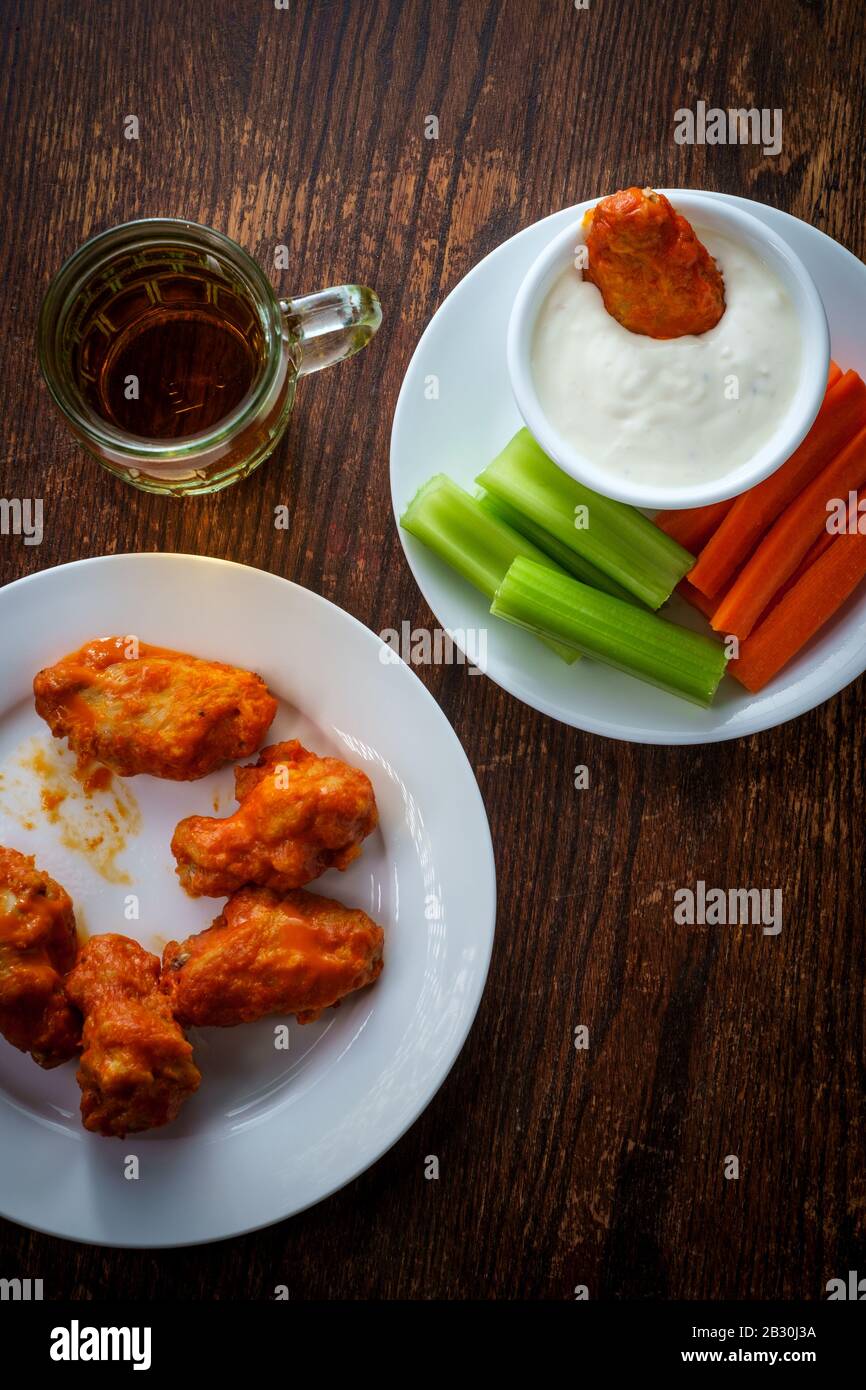 Bar or pub food spicy buffalo wings and beer with sliced carrot sticks ...