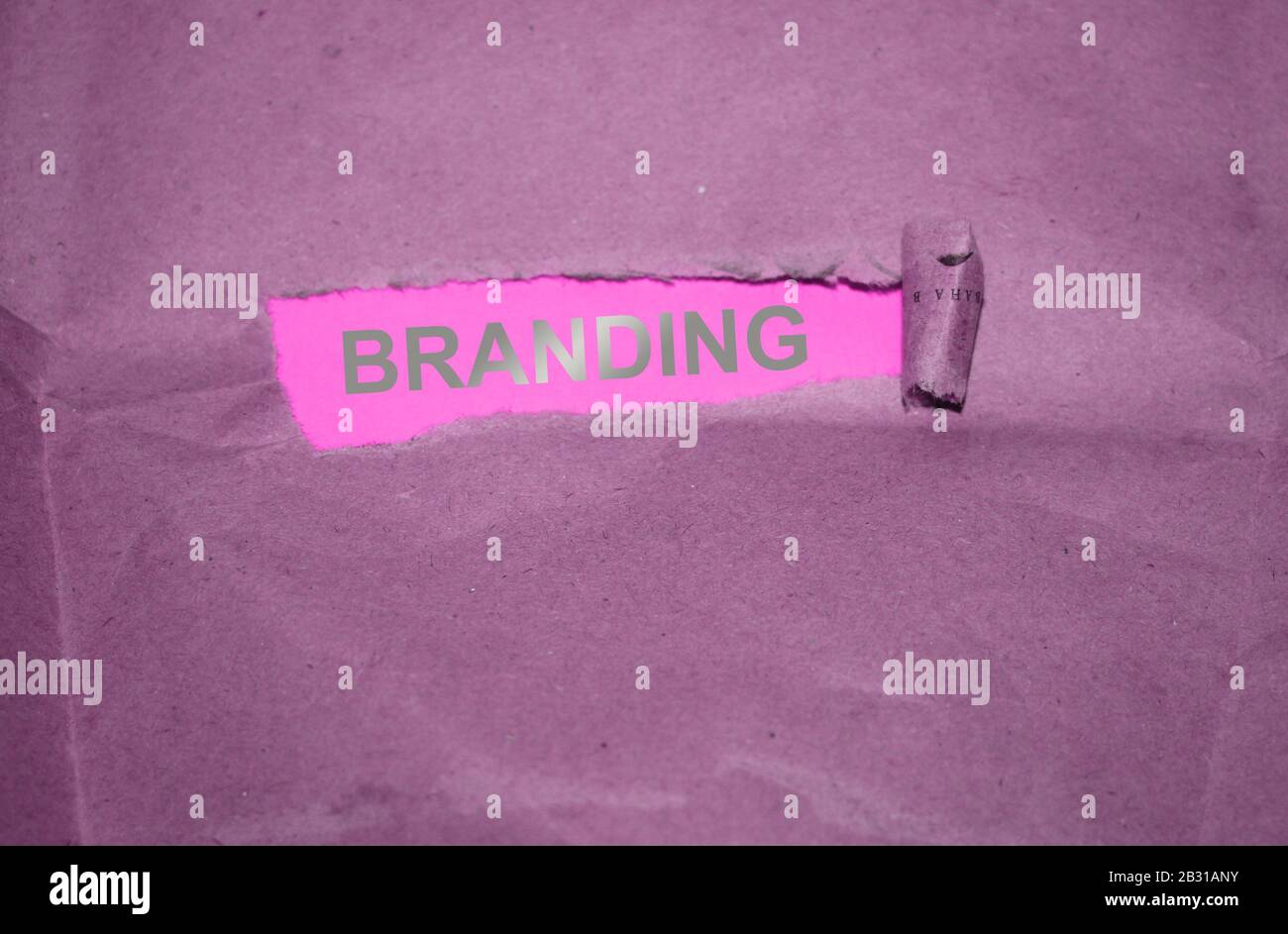 The word Branding written under torn paper with silver letters on pink ...