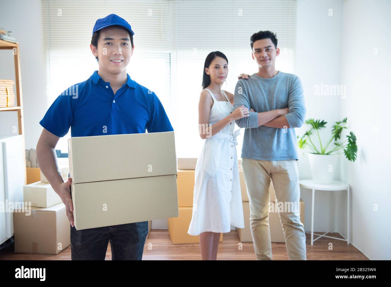 Smiling young asian delivery man in blue uniform holding and carrying ...