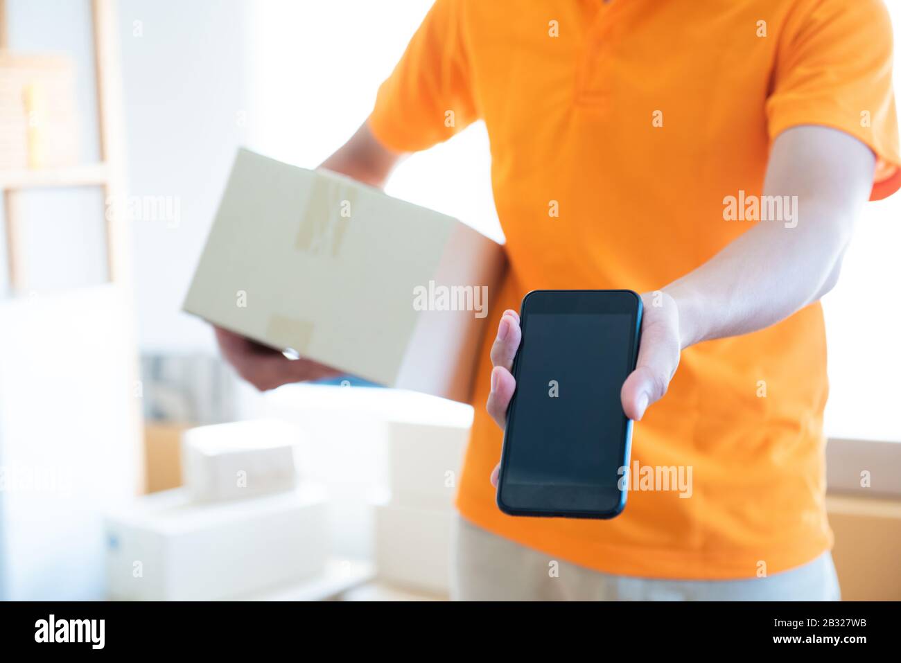 Young delivery man in uniform holding and showing smartphone with blank ...