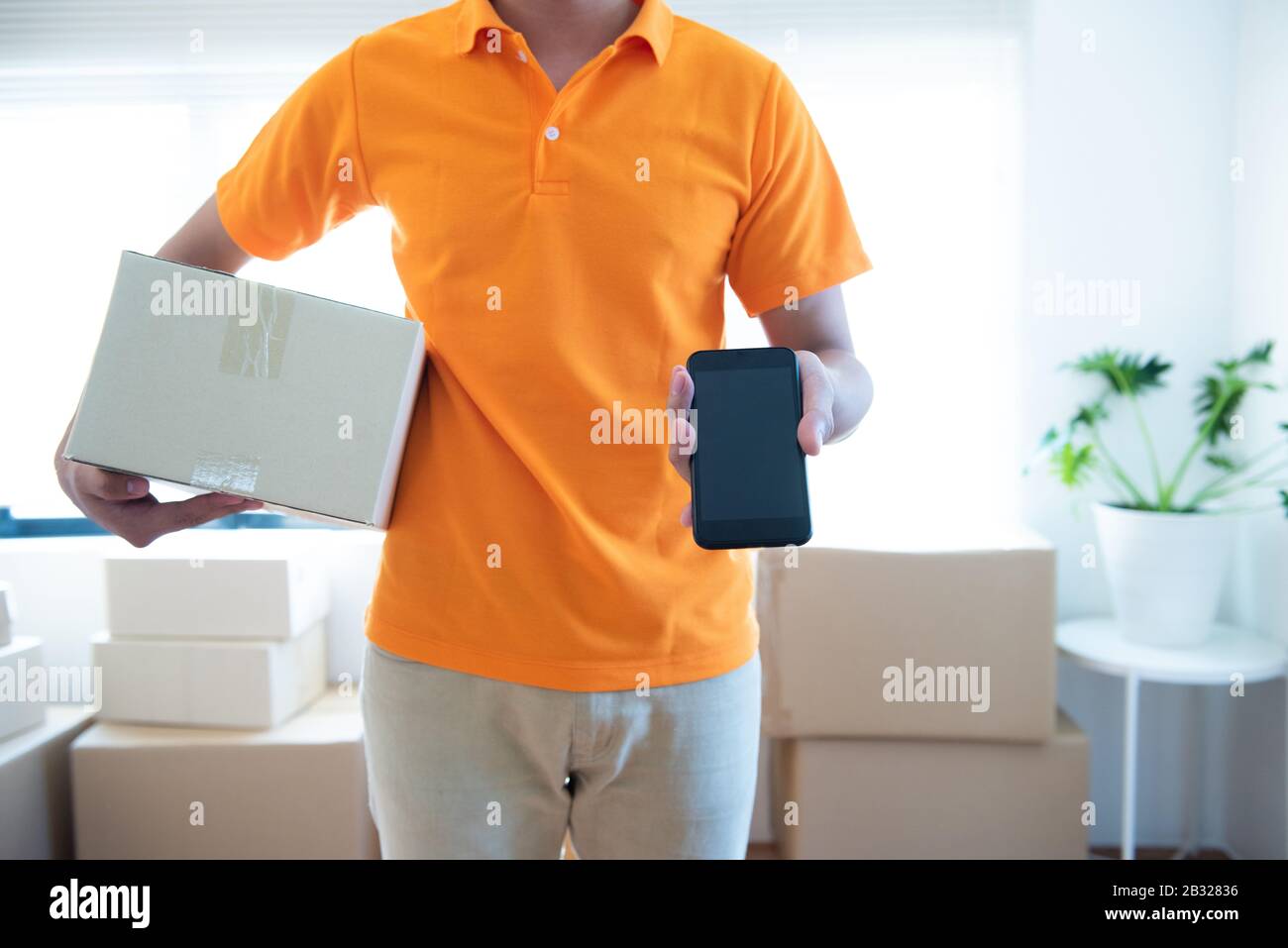 Young delivery man in uniform holding and showing smartphone with blank ...