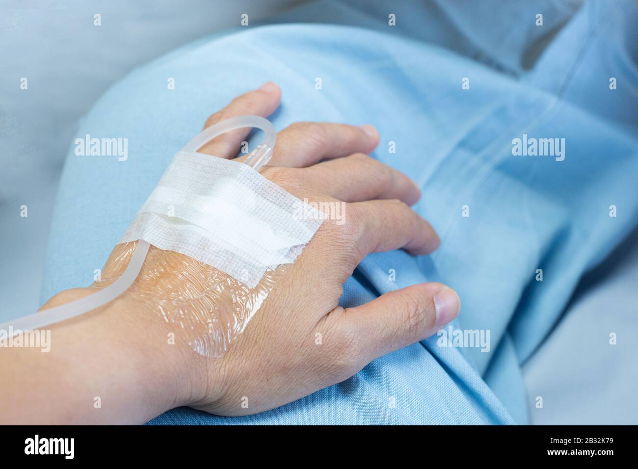 Hand of patient lying on bed in ward at hospital with saline solution ...