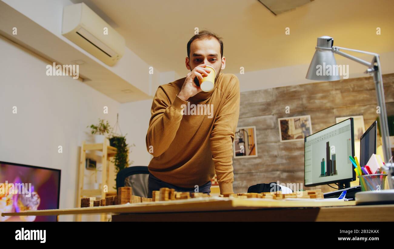 Tired architect taking a sip of coffee while working on a building ...