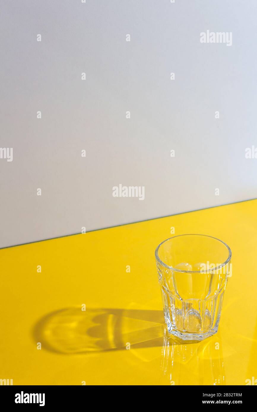 Empty glass with interesting strong hard shadows on yellow background ...