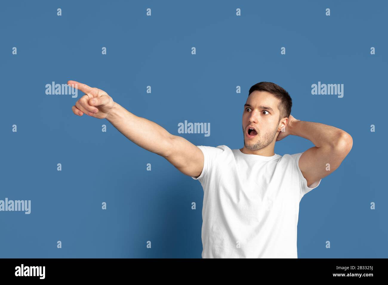 Pointing, choosing. Caucasian young man's portrait isolated on blue ...