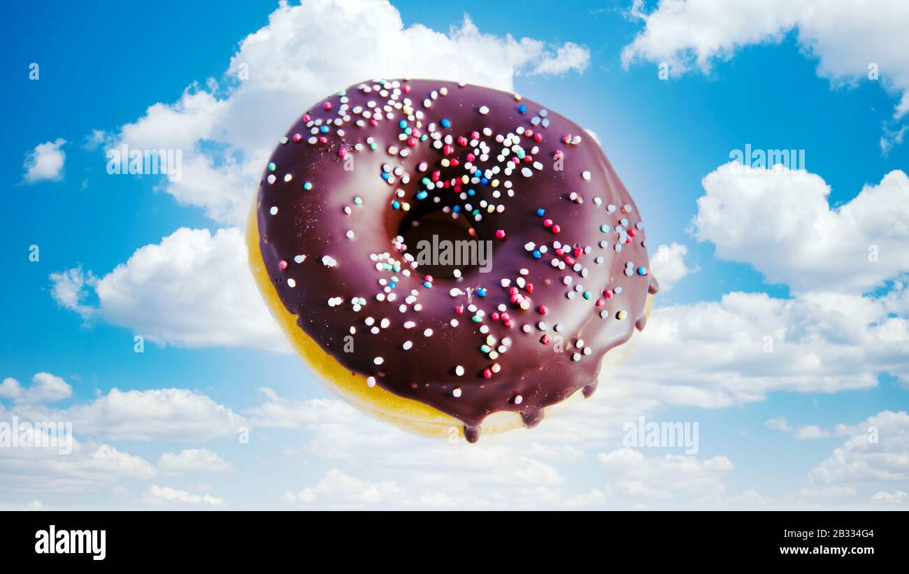 chocolate donut with colorful toppings with blue sky and white clouds ...