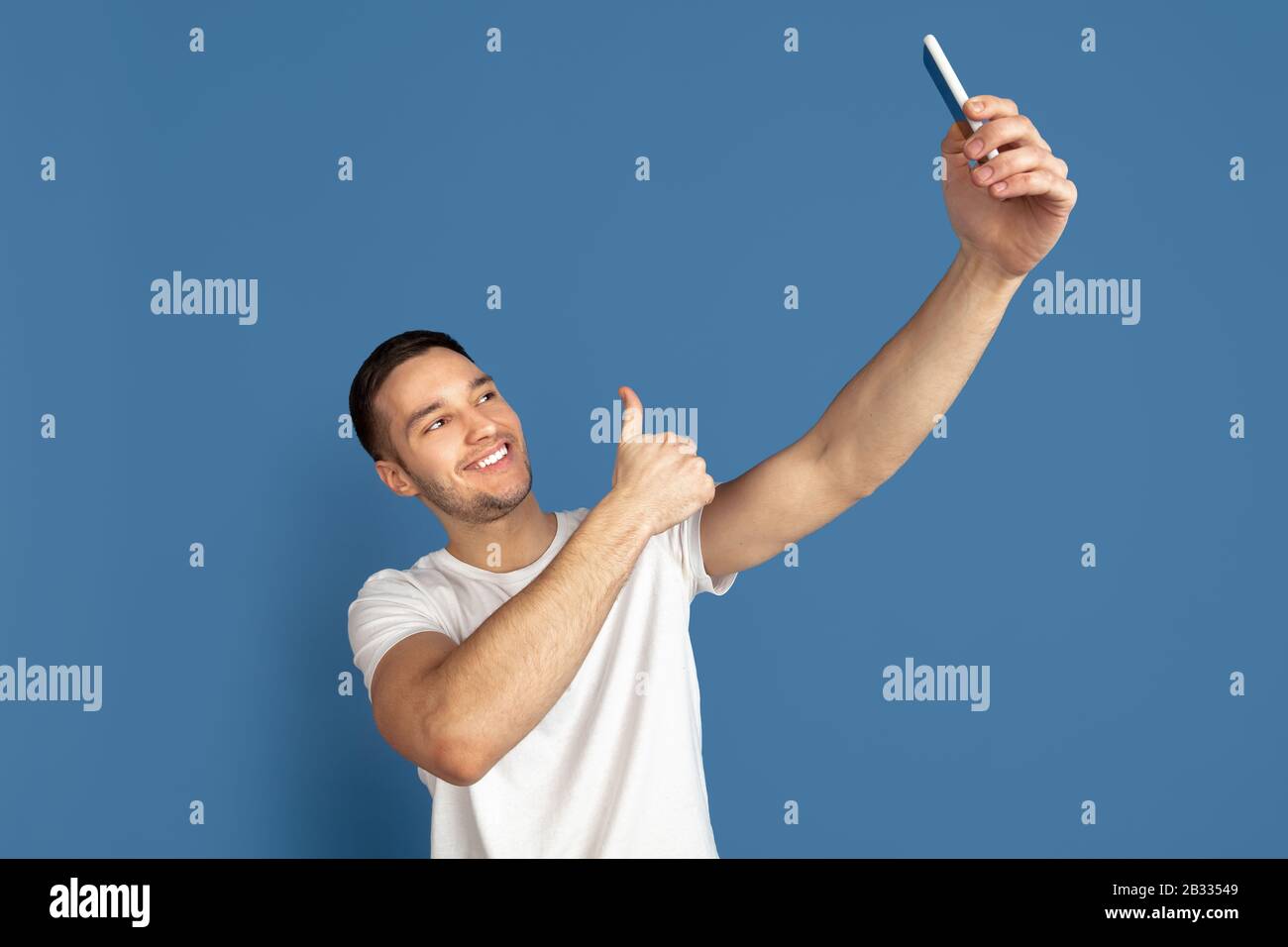Taking selfie. Caucasian young man's portrait isolated on blue studio ...