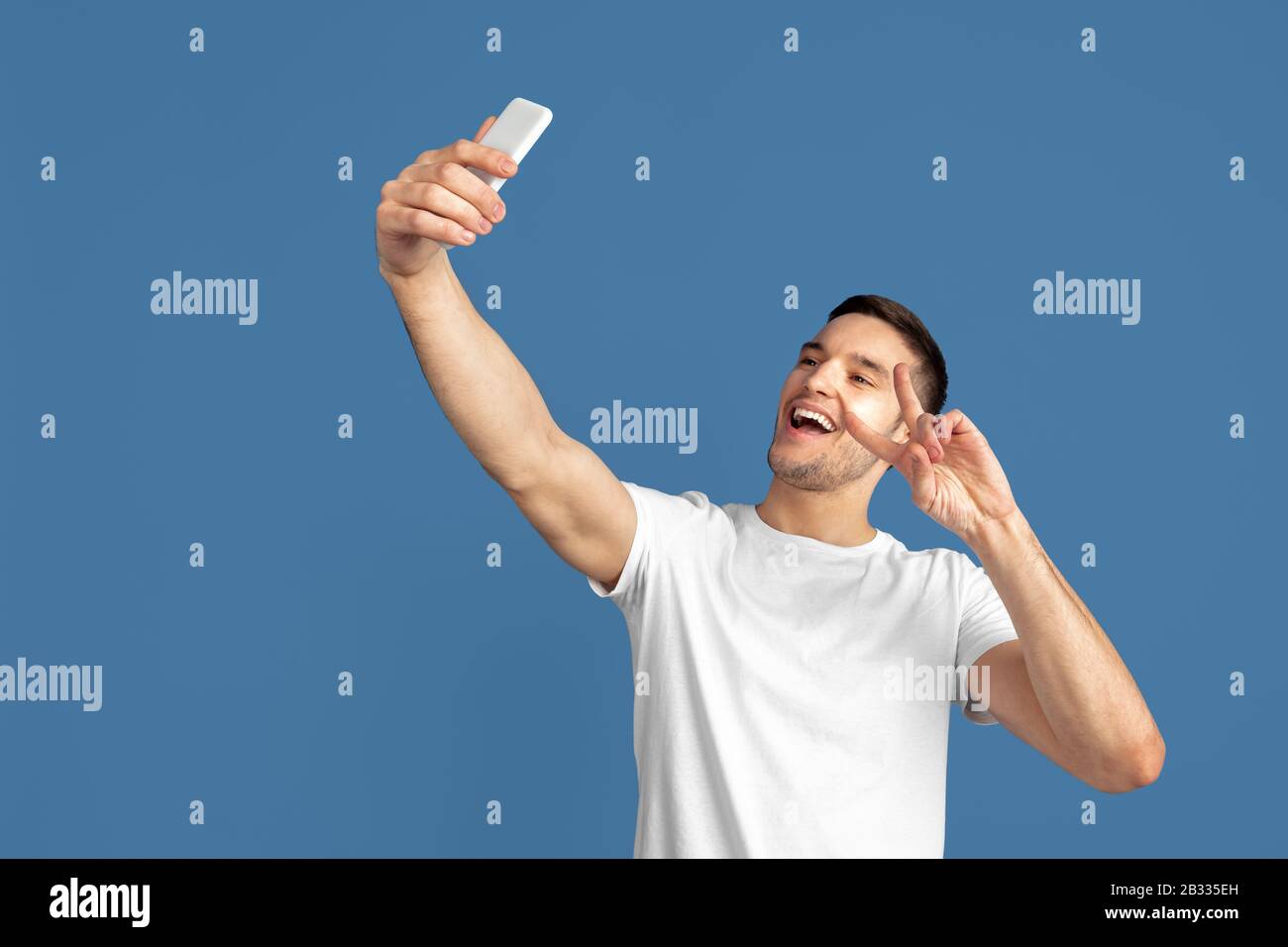 Taking selfie. Caucasian young man's portrait isolated on blue studio ...