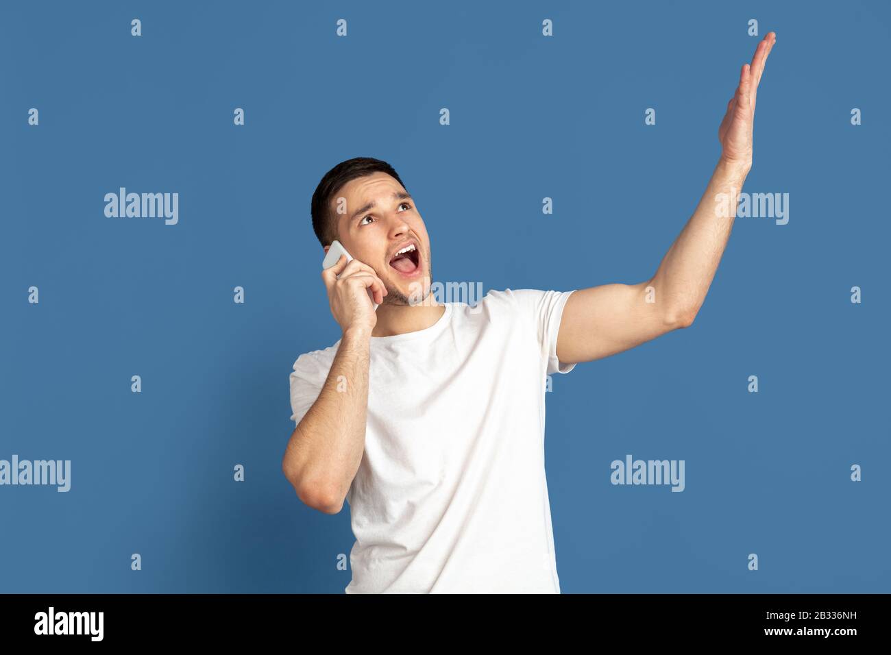 Talking on phone, pointing. Caucasian young man's portrait on blue ...