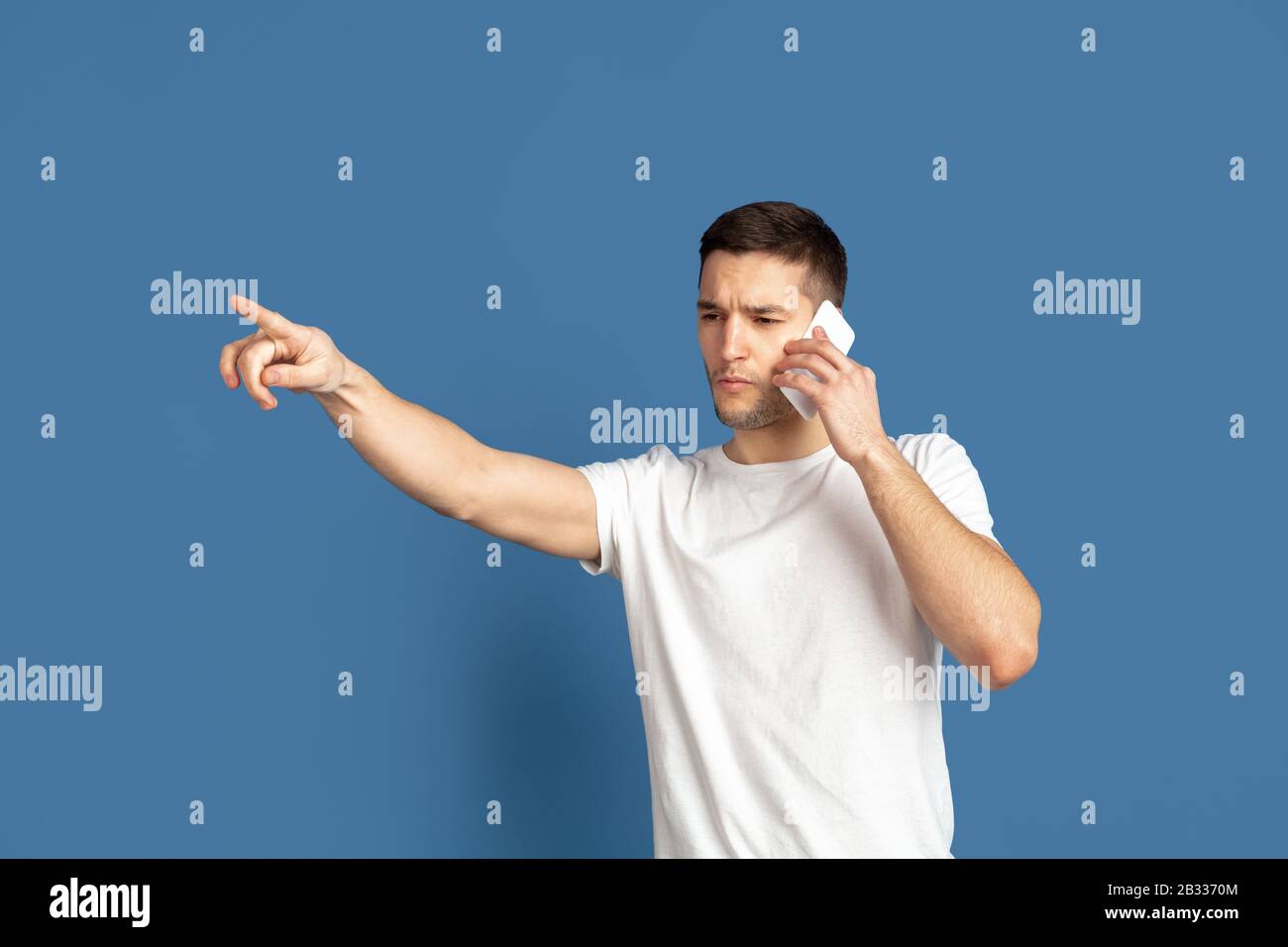 Talking on phone, pointing. Caucasian young man's portrait on blue ...