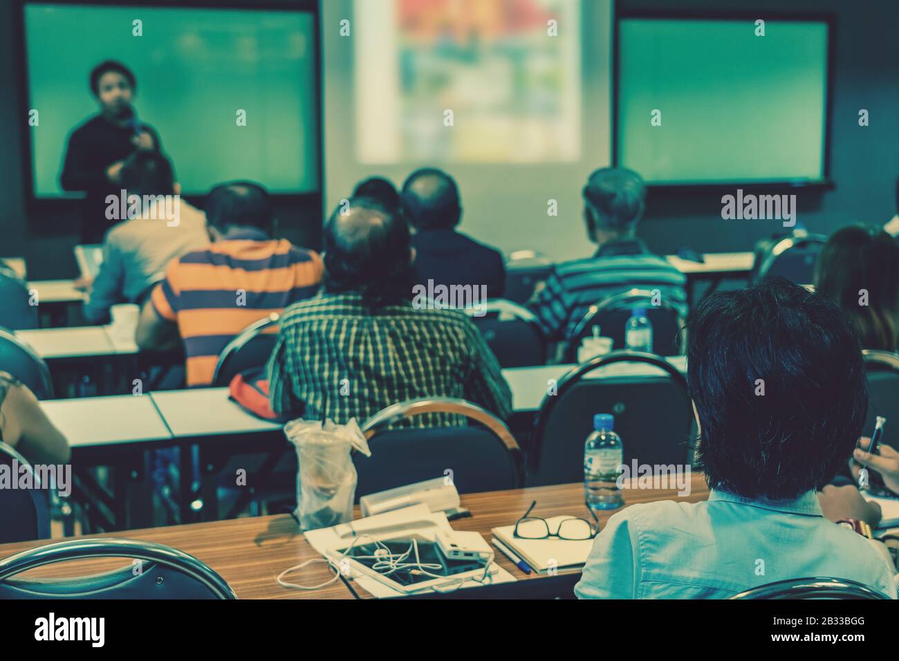 Back side of audience listening the Asian Speaker with casual suit on ...
