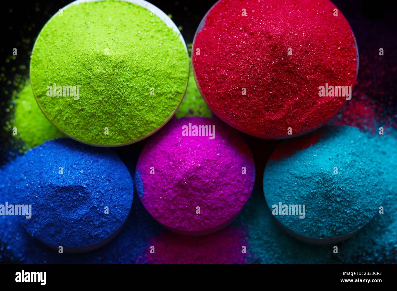 top view of colorful holi powder in bowls isolated on dark backgrounds ...