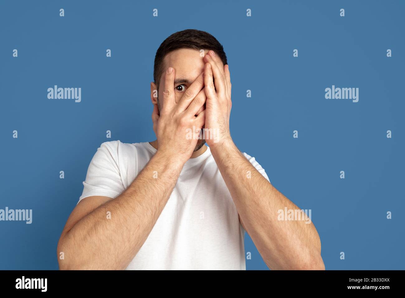 Scared covering face with hands. Caucasian young man's portrait on blue ...