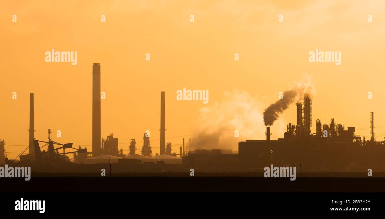 Dutch industrial plant with chimneys and windmill during sunset in ...