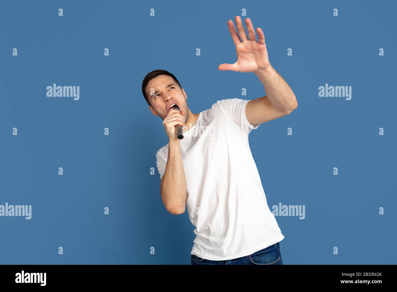 Singing like celebrities, stars. Caucasian young man's portrait on blue ...