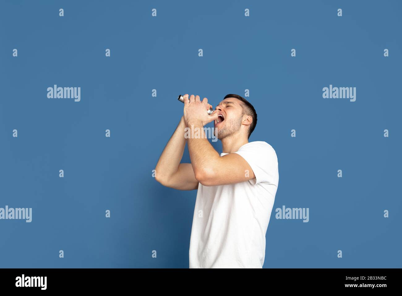 Singing like celebrities, stars. Caucasian young man's portrait on blue ...