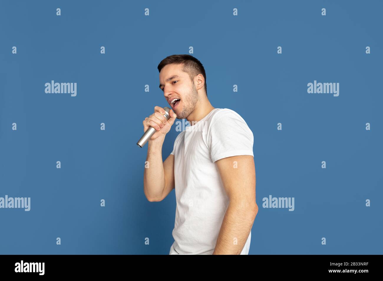 Singing like celebrities, stars. Caucasian young man's portrait on blue ...
