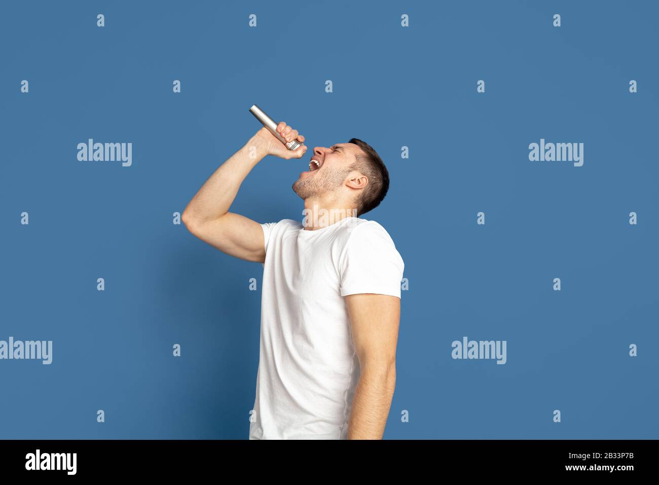 Singing like celebrities, stars. Caucasian young man's portrait on blue ...