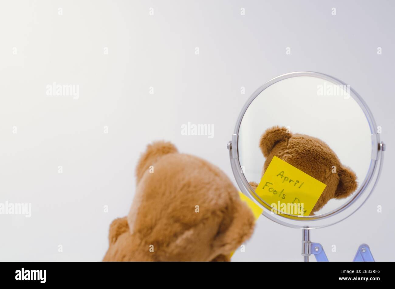 A cute brown teddy bear holding a note with word at mirror for April ...
