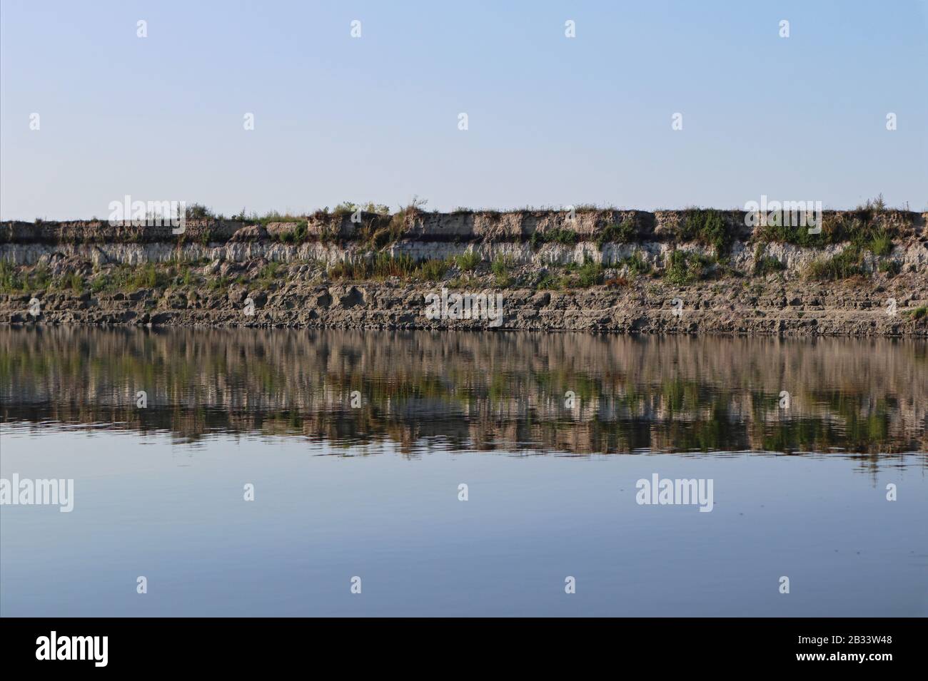 Glass river surface shore hill reflection. Blue sky and water and ...