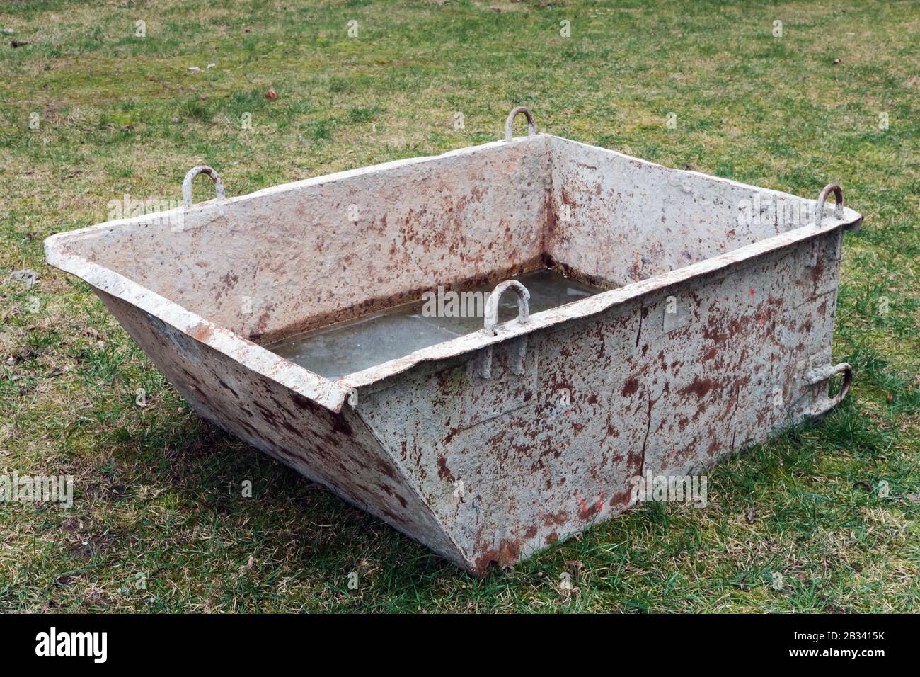 Crumpled rusty iron container for mixing liquid plaster on a grass lawn ...