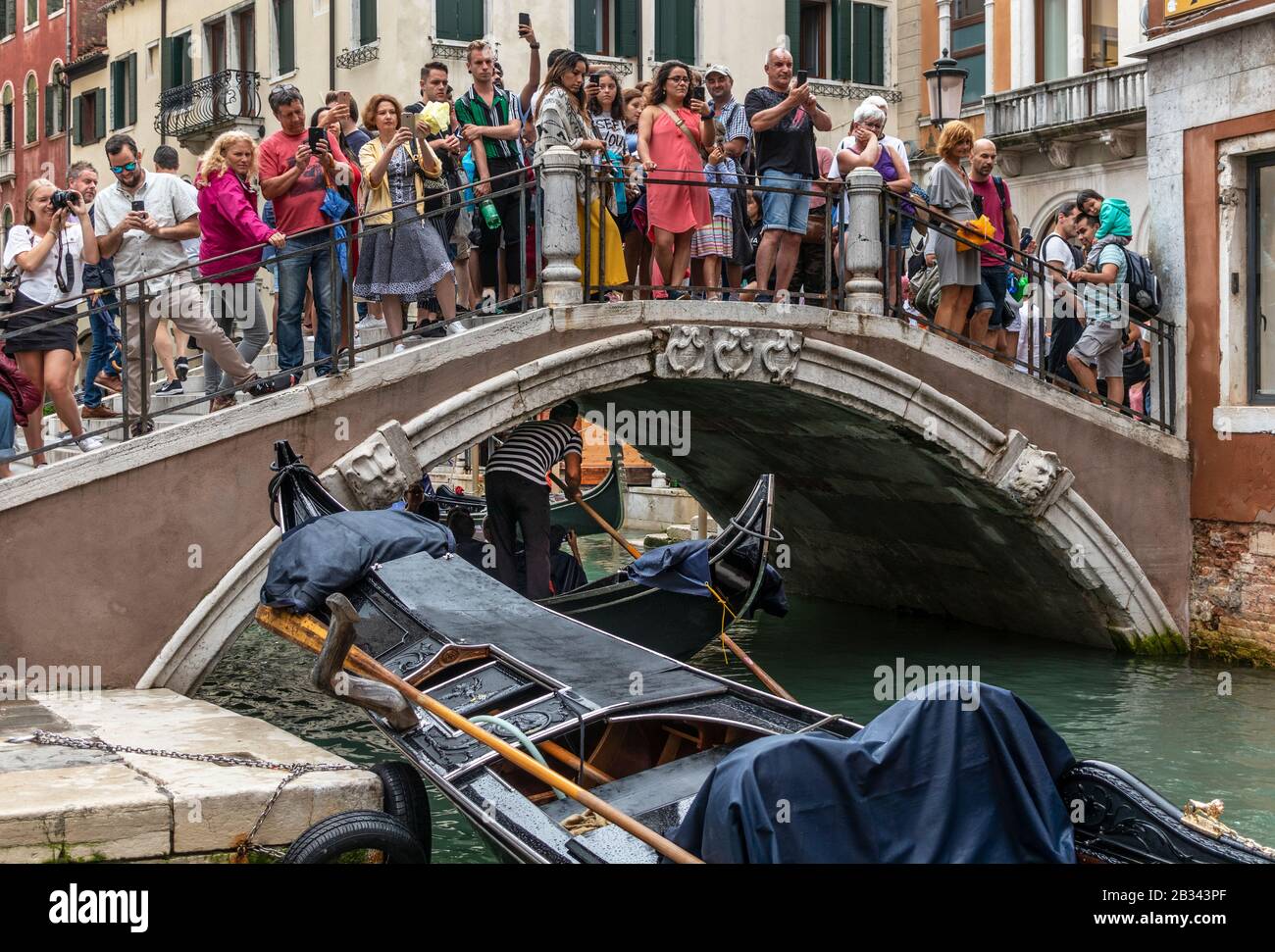 Mass tourism. Crowded bridge over canal, as many tourists watch and ...