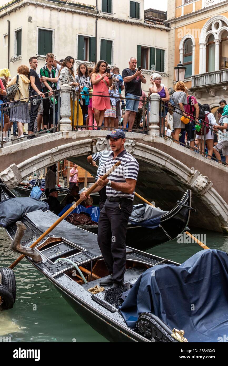 Mass tourism. Crowded bridge over canal, as many tourists watch and ...