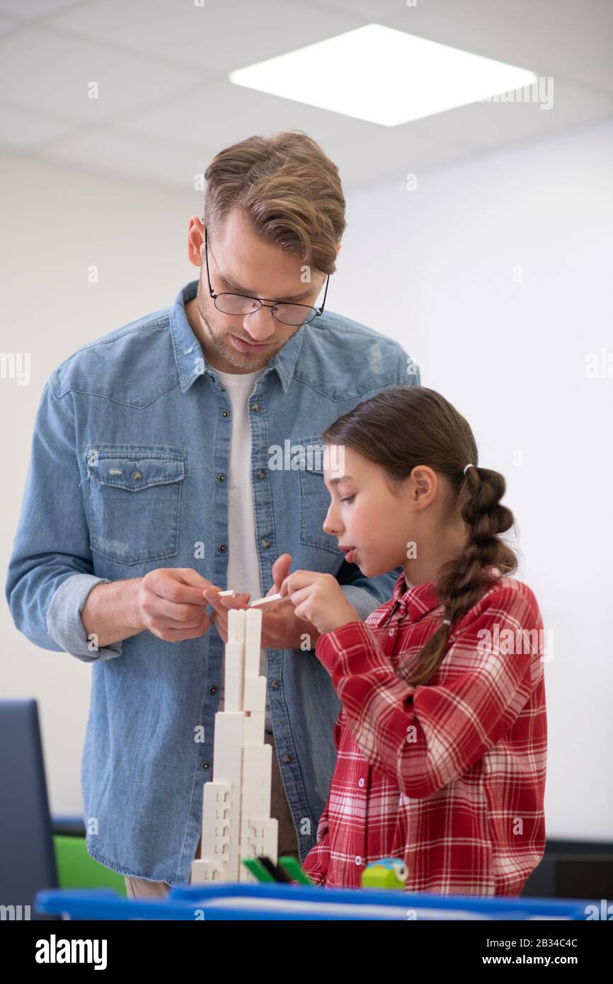 Teacher and girl building tower, attaching blocks Stock Photo - Alamy