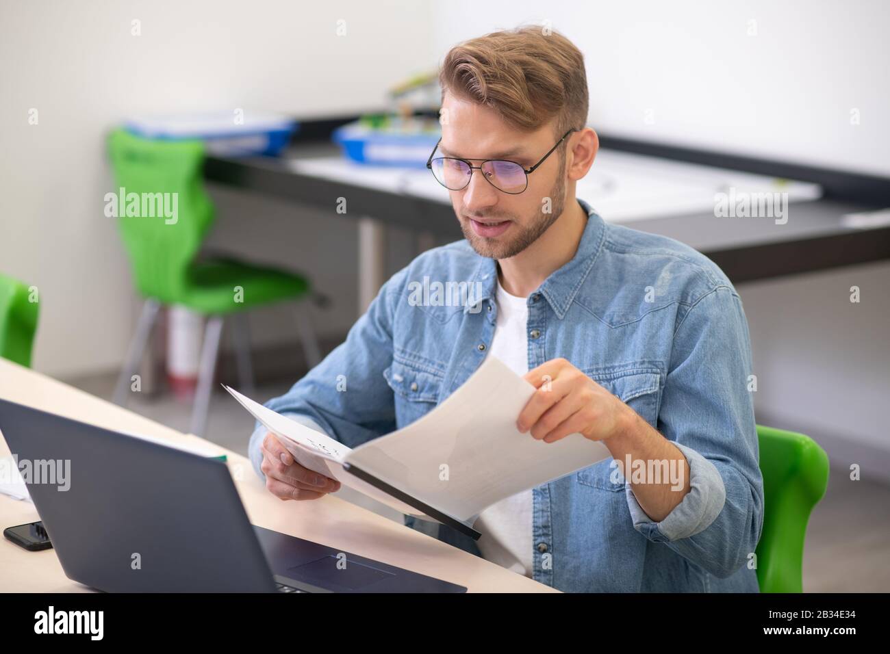 Male teacher sitting at laptop, checking notes Stock Photo - Alamy