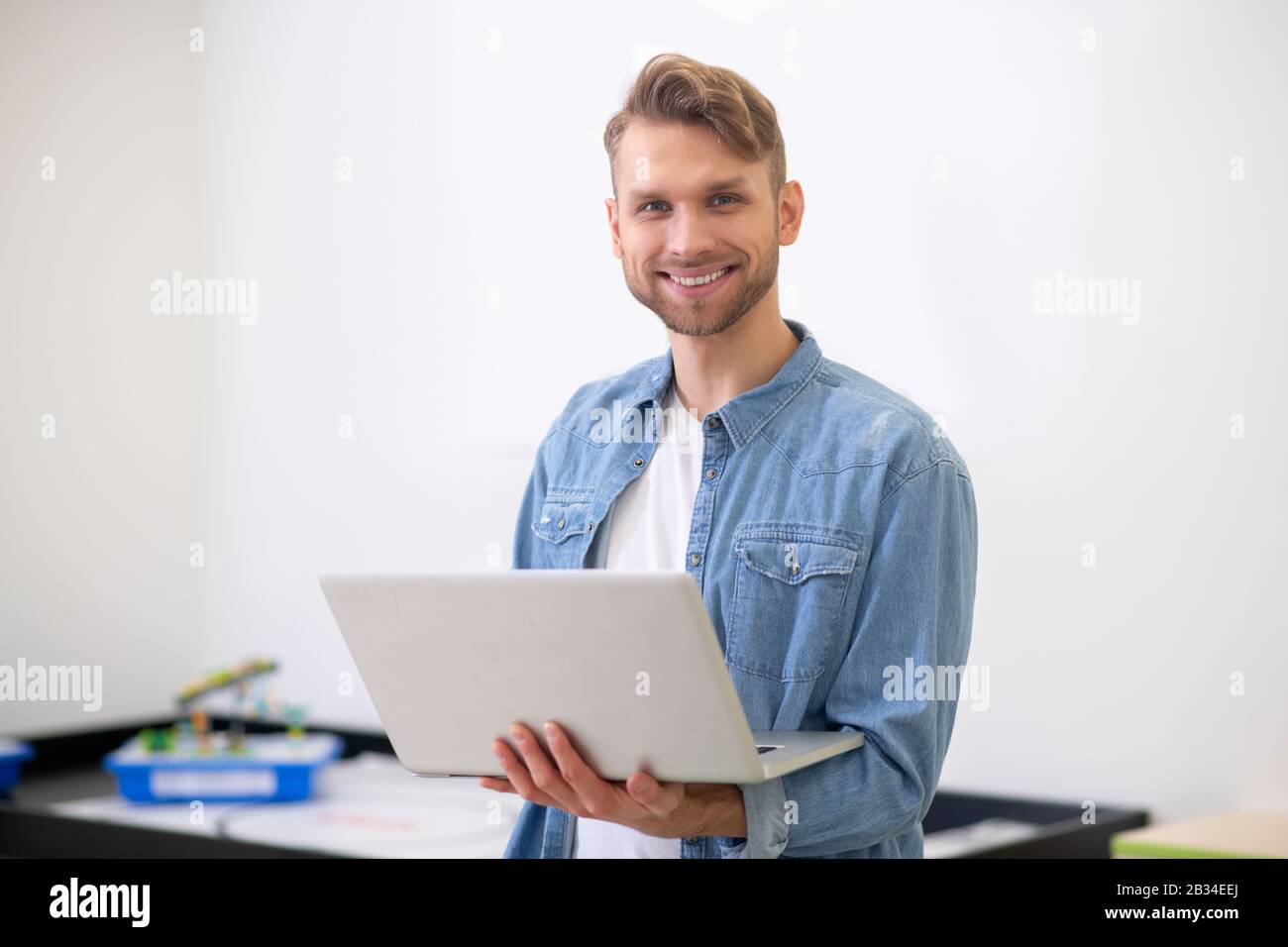 Male teacher standing, holding laptop and smiling Stock Photo - Alamy