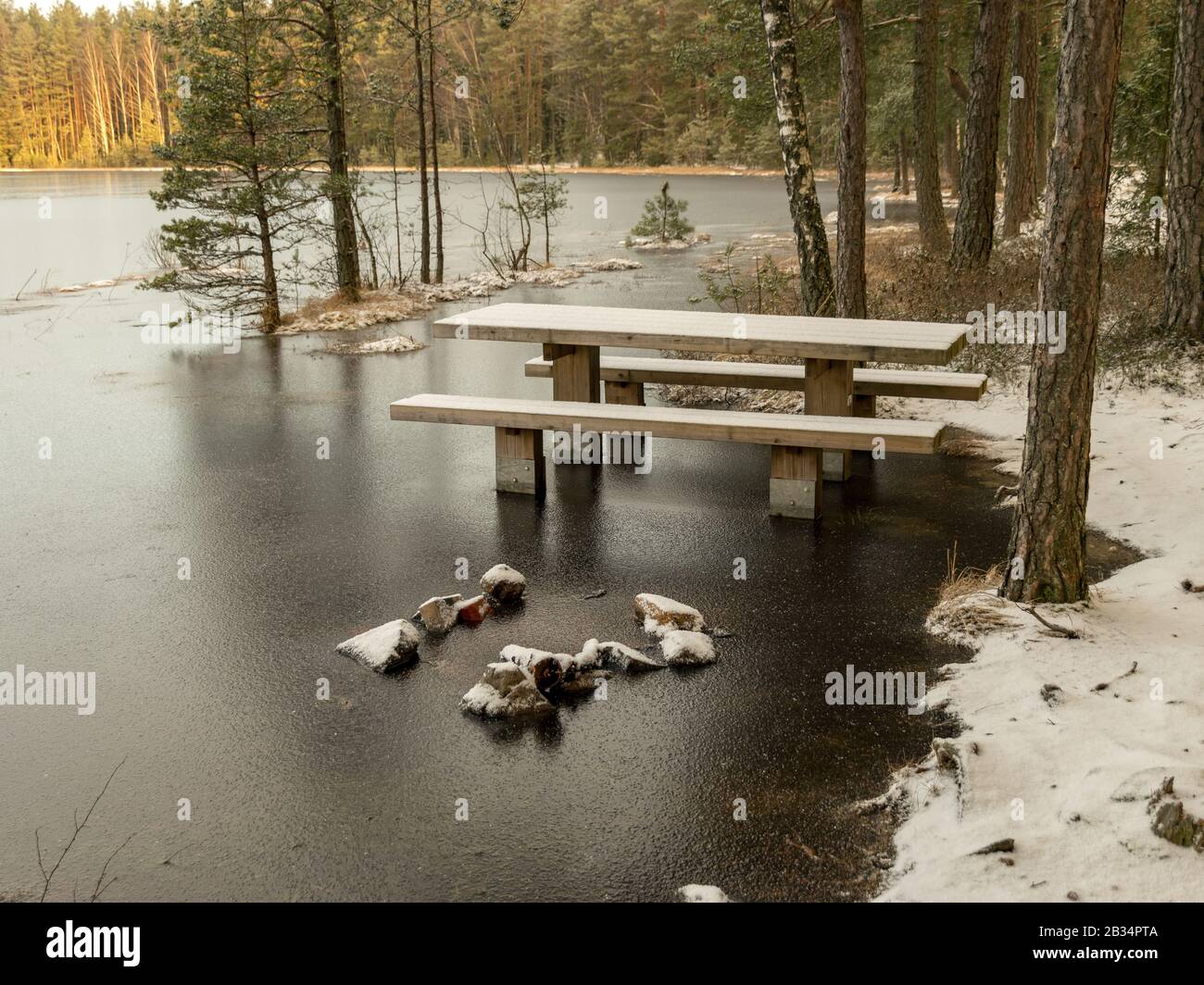 winter landscape with flooded lake shore, picnic area covered with ice ...