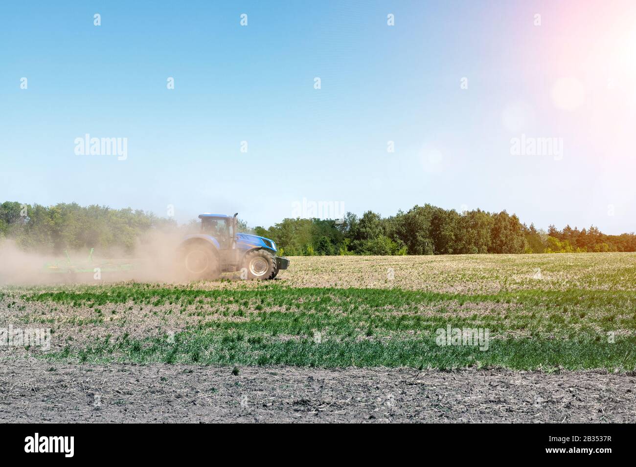 Blue modern tractor covered with earth dust plowing agricultural field ...