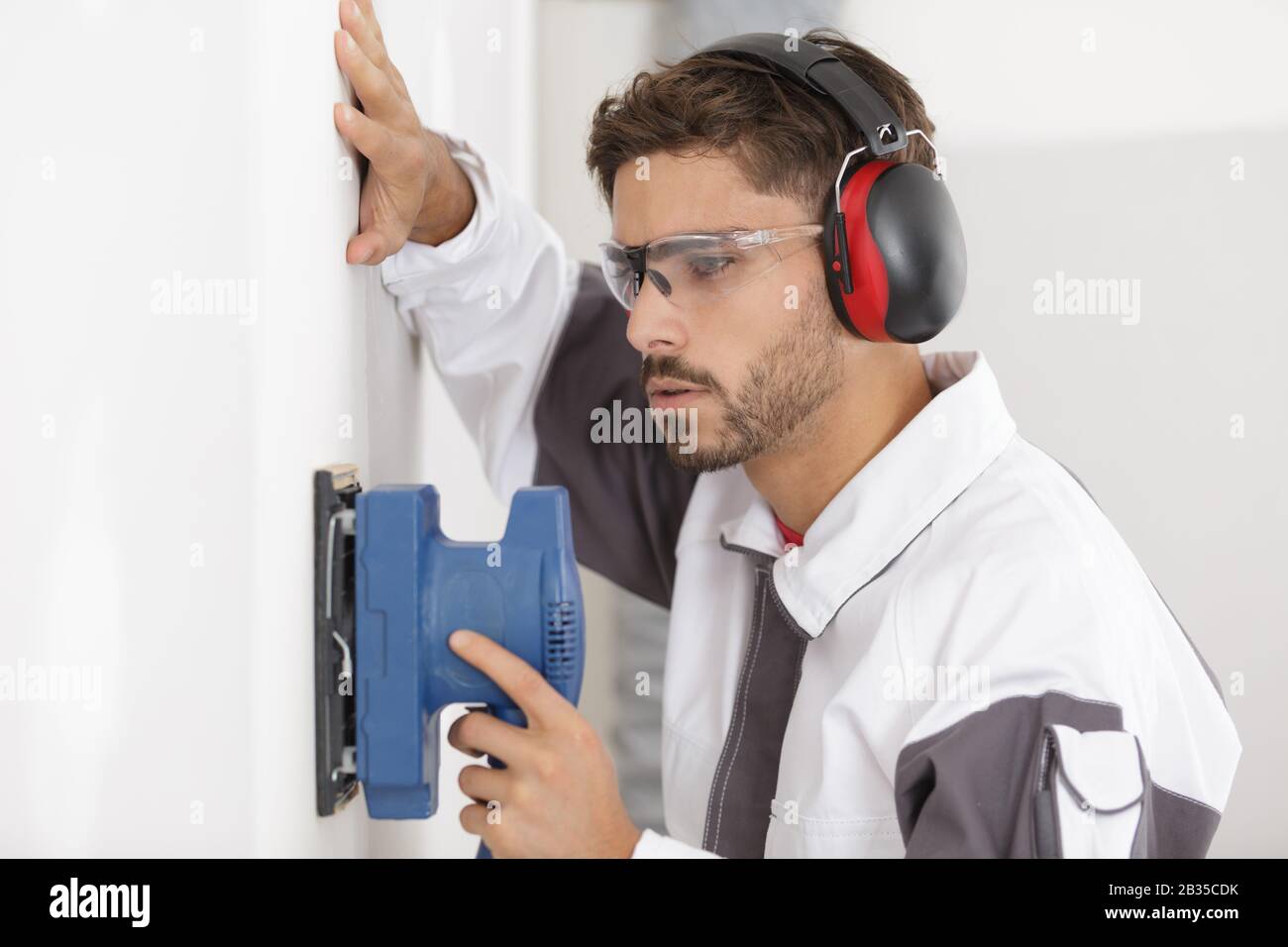 young male worker sanding the wall Stock Photo - Alamy