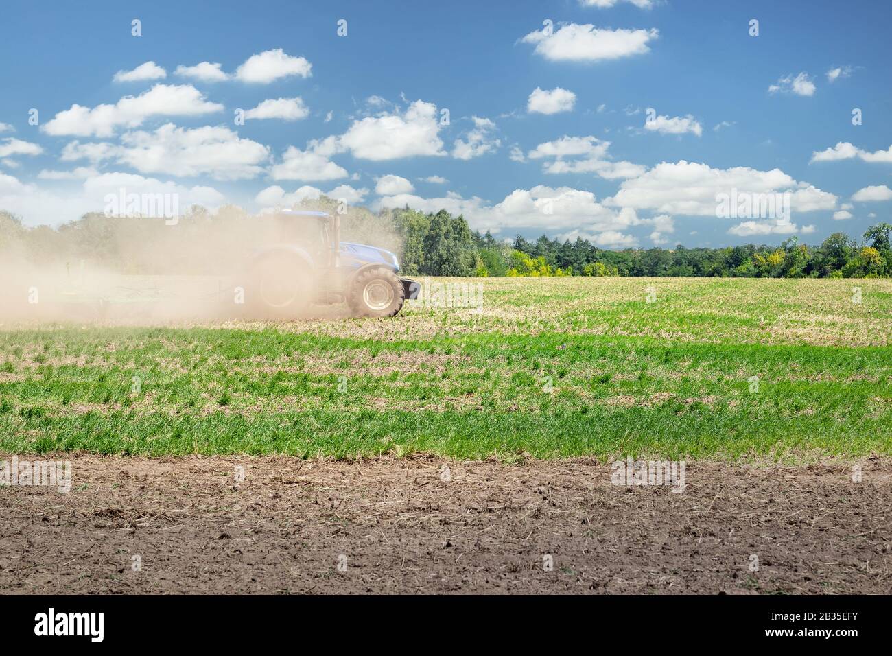 Blue modern tractor covered with earth dust plowing agricultural field ...