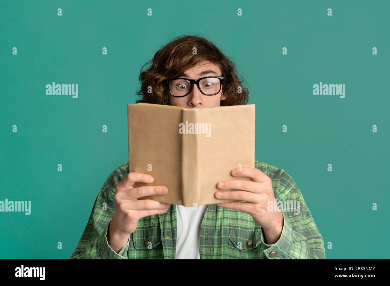 Education concept. Puzzled young man with glasses reading book on color ...