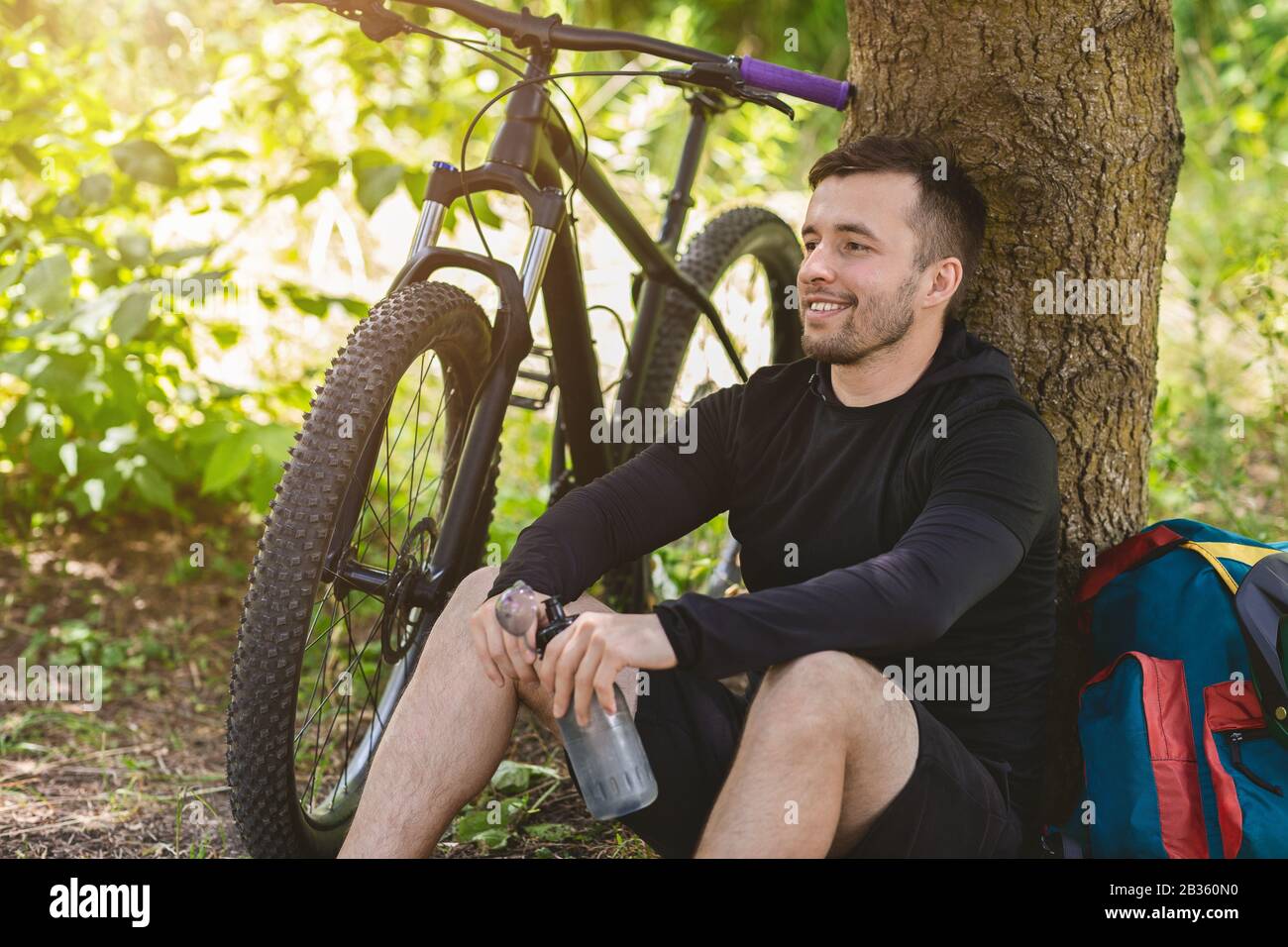 Smiling cyclist resting under tree in mountain forest Stock Photo - Alamy