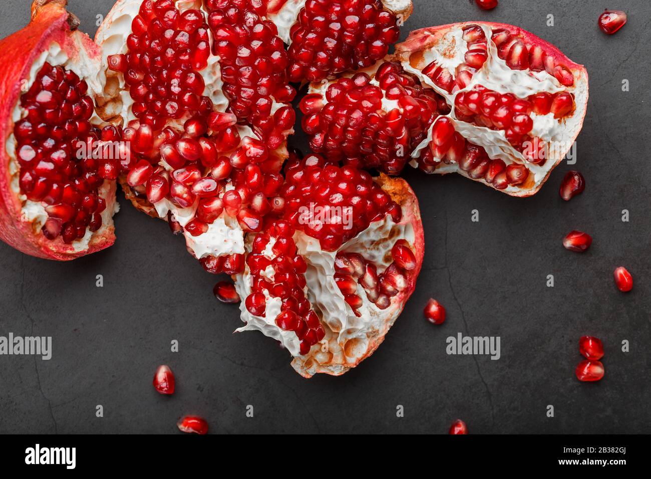The opened Fruits of a ripe open pomegranate lie on a black textural ...